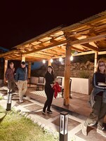 Um espaço ao ar livre coberto com paredes de pedra e vigas de madeira, apresentando um banco de pedra e uma mesa.