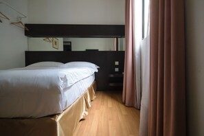 Uma cama de solteiro com cabeceira, chão de madeira e janela com cortinas.