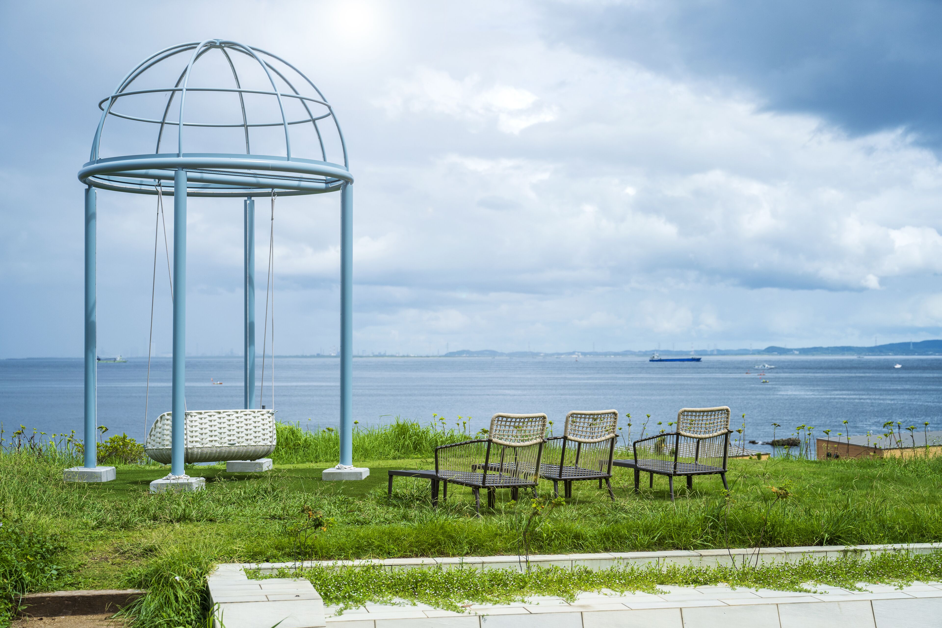 Um gazebo com vista para o mar, duas cadeiras de vime e um balanço.