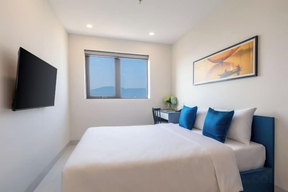 Quarto de hotel com cama, televisão de tela plana, janela e pintura na parede.