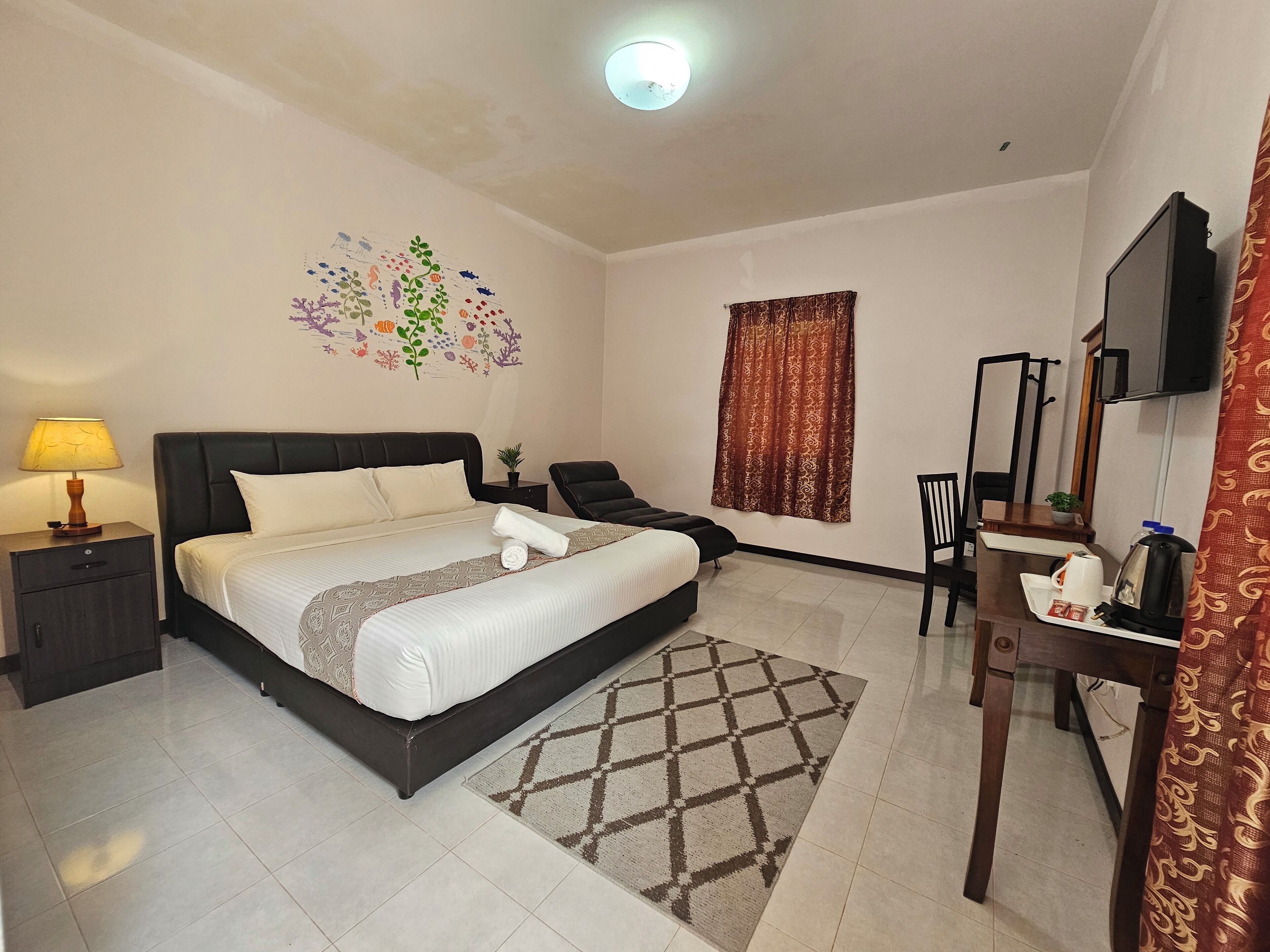 Quarto de hotel com cama, escrivaninha, cadeira, televisão e um objeto decorativo na parede.