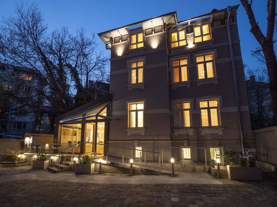 Um edifício de vários andares com janelas iluminadas e uma área de entrada coberta, com degraus e assentos.