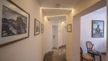 Corredor com fotografias históricas emolduradas, sinal de saída e área de refeições com uma cadeira e mesa.