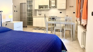 Quarto de hotel compacto com cama, pequena escrivaninha, cozinha compacta e área de refeições.