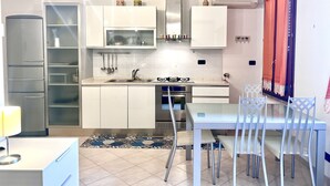 Cozinha moderna com armários brancos, fogão a gás e área de refeições com cadeiras brancas.