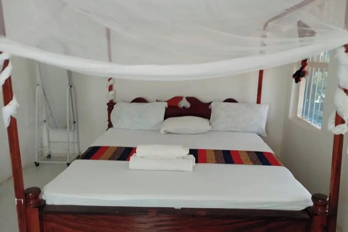 Cama com dossel, almofadas, colcha listrada e toalha branca.
