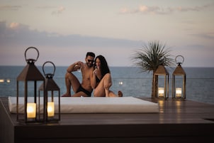 Um casal sentado em um deque com vista para o mar, rodeado por lanternas e velas.