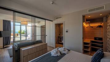 Quarto de hotel moderno com uma cama grande, área de estar, closet espaçoso e vista através de um painel de vidro.