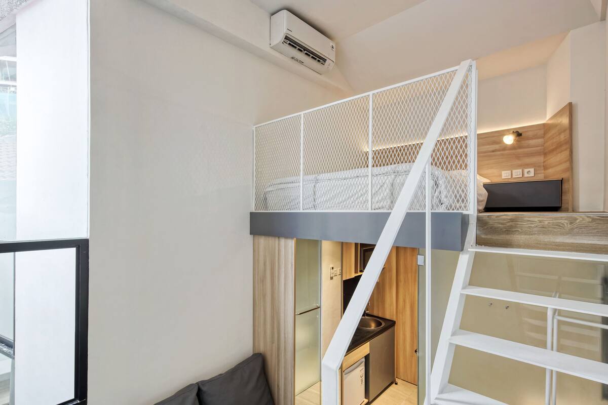 Quarto moderno no estilo loft, com beliche, pequeno espaço de cozinha e sofá.