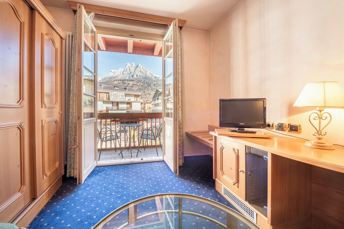 Quarto de hotel com varanda, televisão e candeeiro.