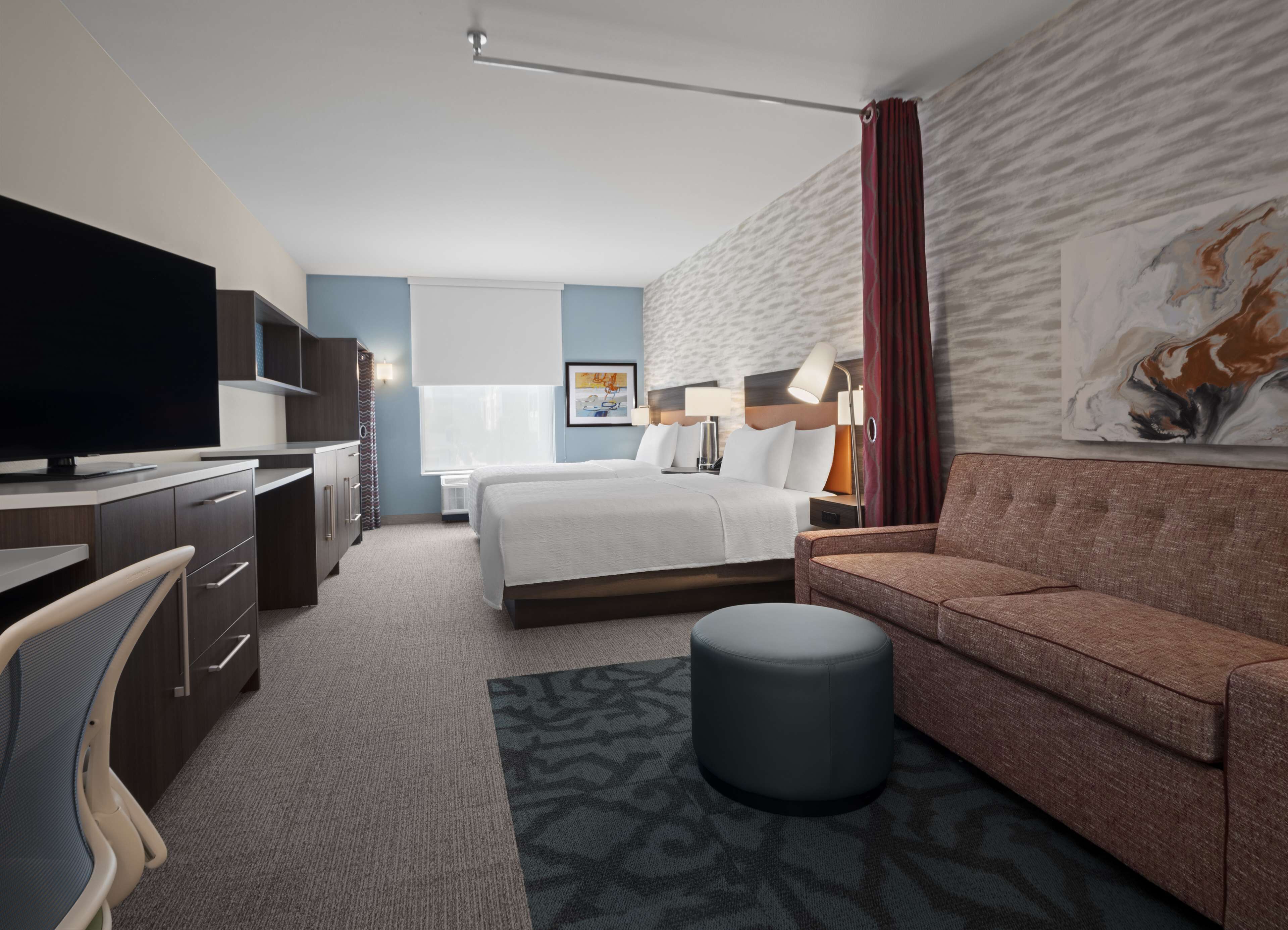 Quarto de hotel com cama, escrivaninha, televisão, sofá e um quadro na parede.