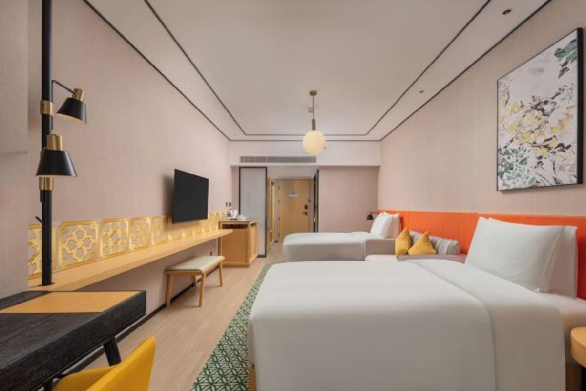 Quarto de hotel com duas camas, uma escrivaninha com cadeira, televisão e um quadro na parede.