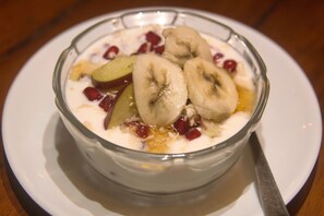 Uma tigela de iogurte com fatias de banana e sementes de romã sobre um prato branco.