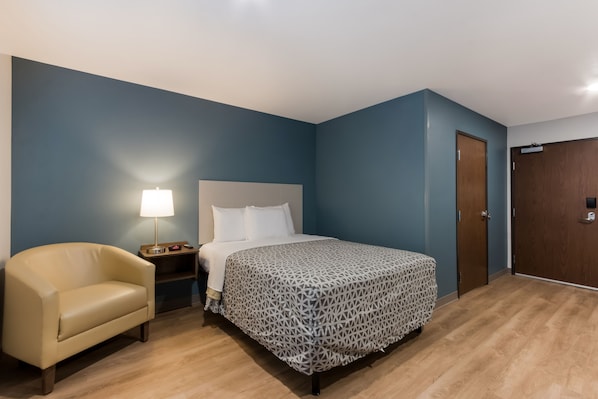 Um quarto com cama, mesa de cabeceira, luminária, cadeira e guarda-roupa.