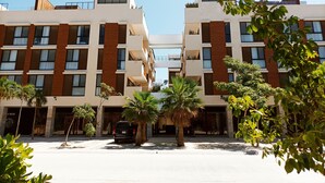 Um hotel moderno com fachada simétrica, várias varandas e um pátio central com palmeiras.