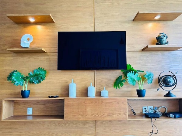 Uma sala de estar moderna com televisão na parede, prateleiras de madeira e plantas decorativas.