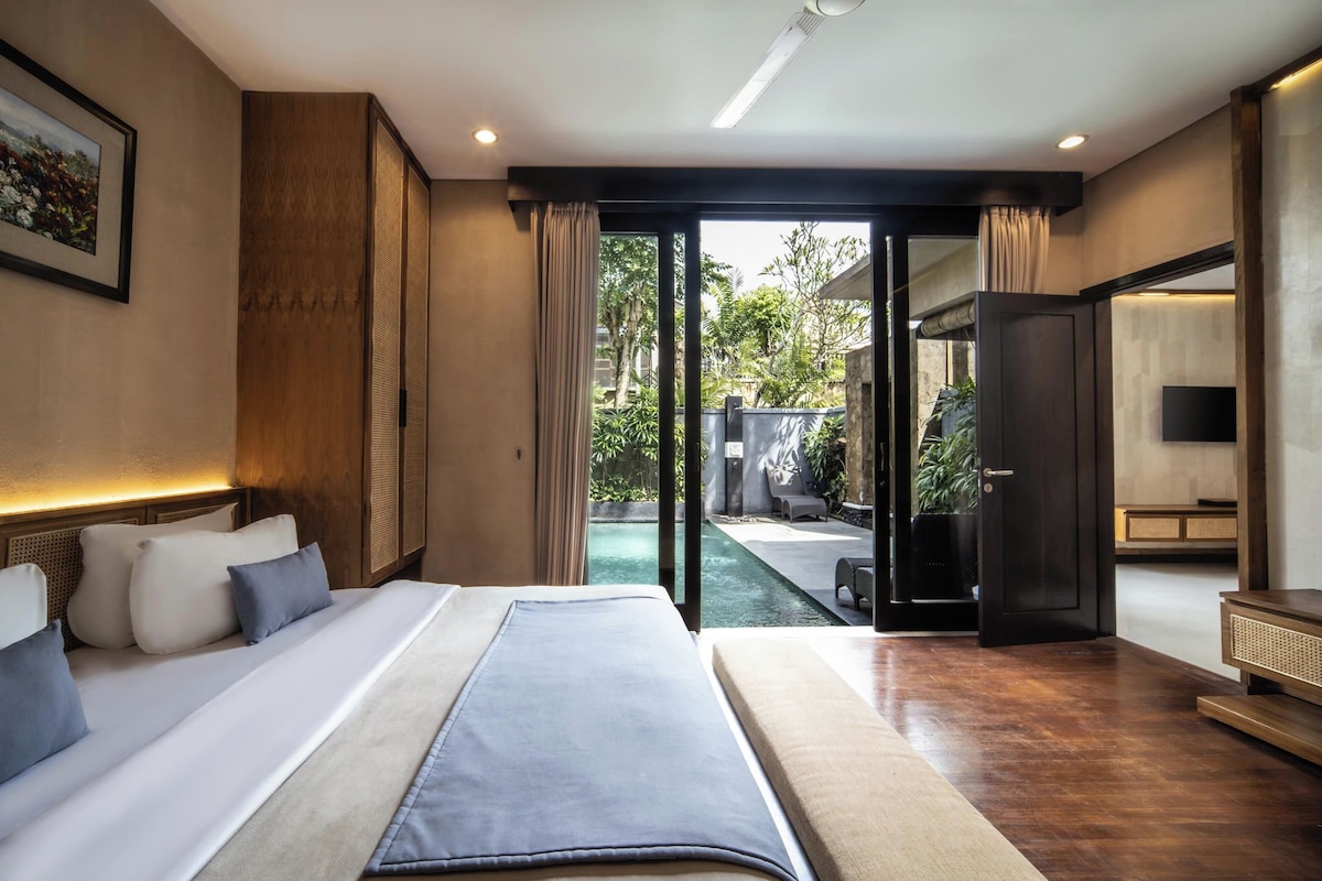 Quarto moderno com uma cama grande, televisão e vista para um jardim.