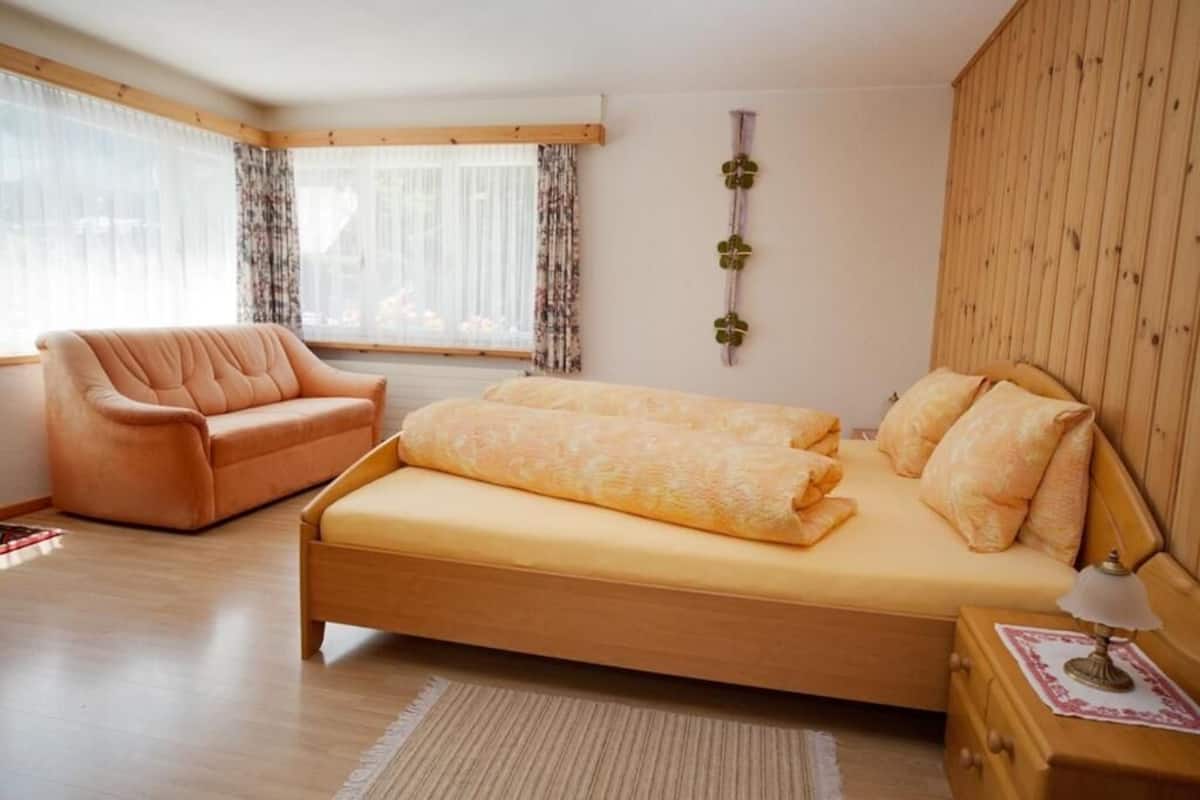 Quarto com uma cama, uma cadeira e uma janela com cortinas.