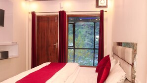 Quarto com uma cama grande, janela com cortinas e vista para árvores.