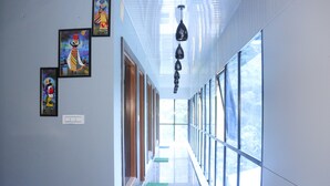 Um corredor com amplas janelas, obras de arte nas paredes e um lustre.