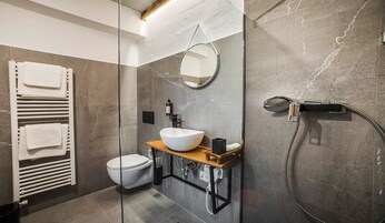 Uma casa de banho moderna com chuveiro em cabine de vidro, lavatório branco e porta-toalhas.