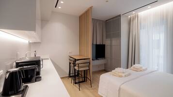 Quarto de hotel moderno com cama, escrivaninha com cafeteira, televisão e janela com cortinas.