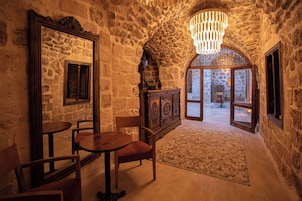 Um quarto com paredes de pedra, um candelabro, um armário de madeira e um espelho.