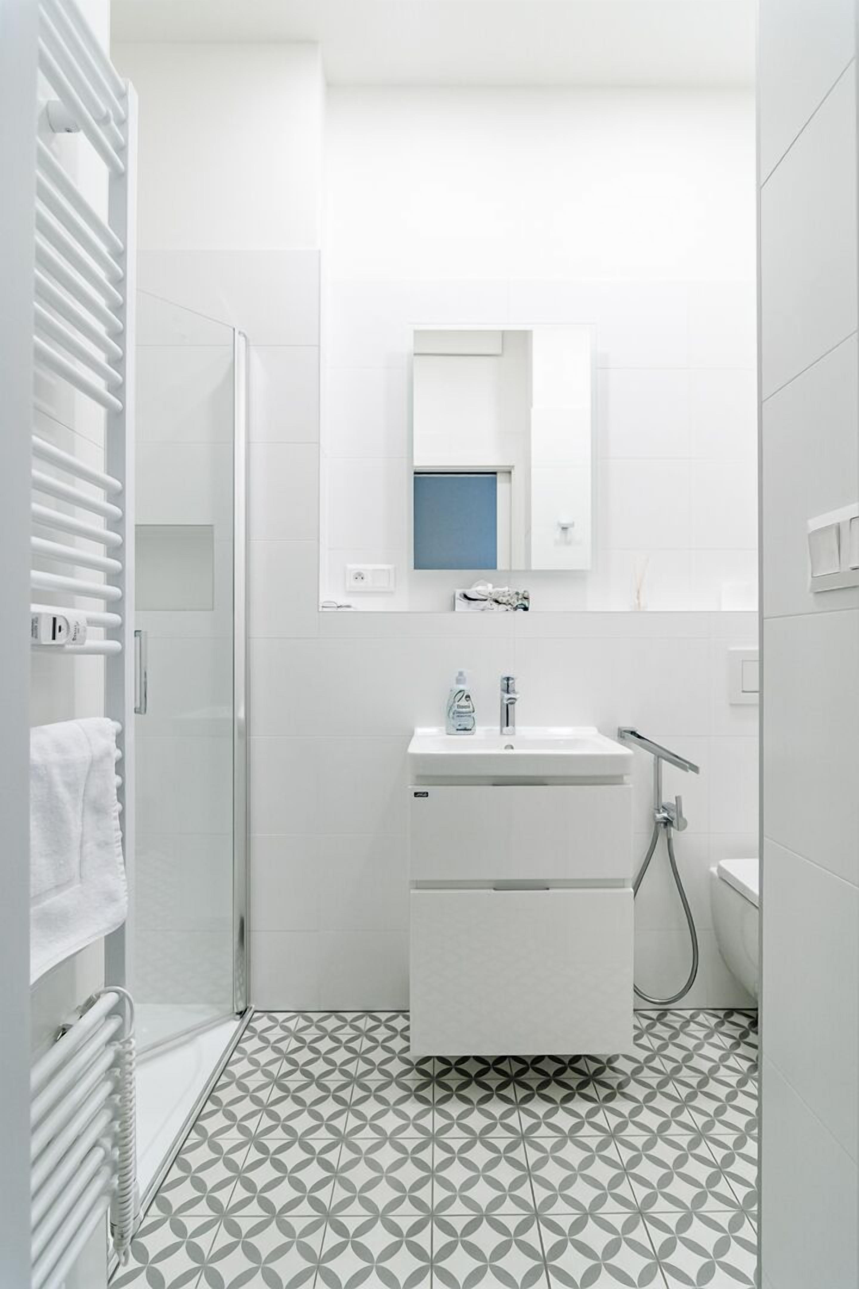 Um banheiro moderno com box de vidro, pia branca com espelho acima e piso em azulejos estampados.