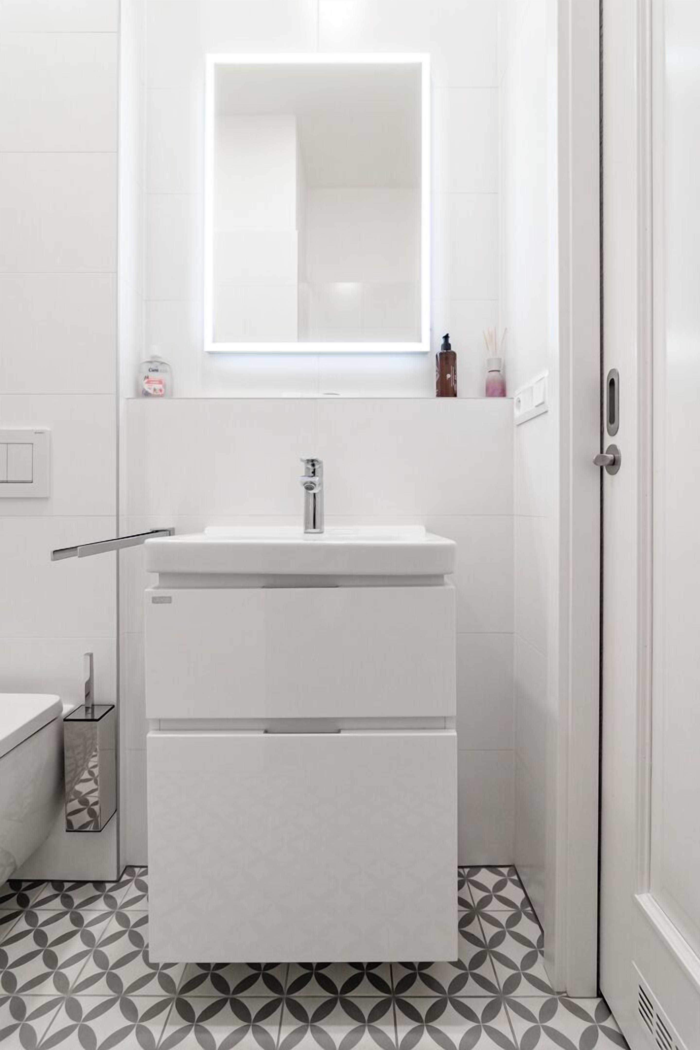 Casa de banho moderna com lavatório branco, espelho e chão em azulejos.