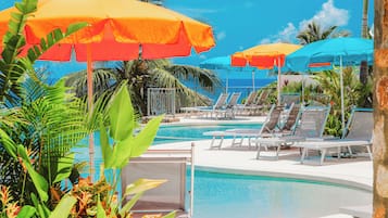 Uma área à beira da piscina com espreguiçadeiras e guarda-sóis, cercada por plantas tropicais.