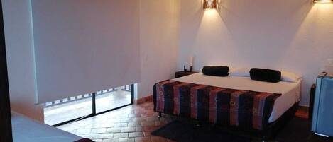 Quarto com cama, mesa de cabeceira, luminária na parede e janela com vista para o exterior.