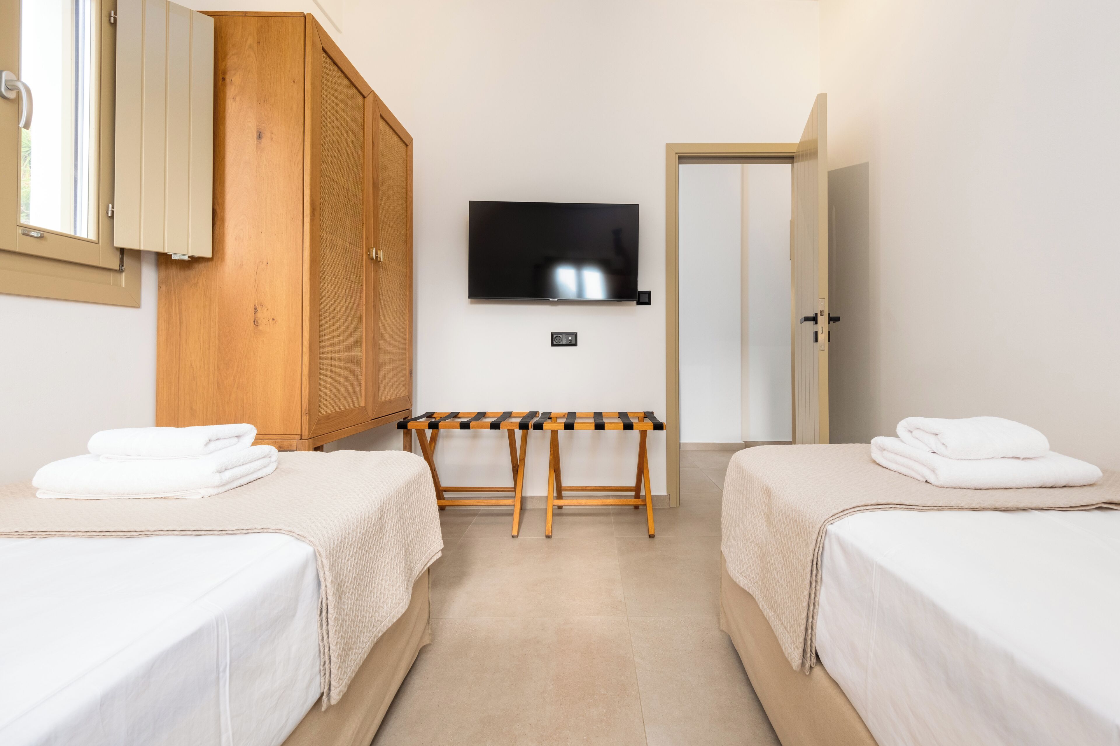 Quarto de hotel com duas camas, um guarda-roupa de madeira, uma televisão e uma pequena mesa.