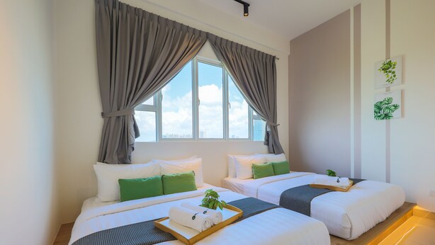 Quarto de hotel com duas camas, cortinas cinzentas, uma janela grande e uma planta na mesa de cabeceira.