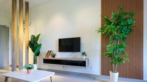 Sala de estar moderna com televisão de tela plana na parede, uma mesa branca com uma cadeira e várias plantas em vasos.