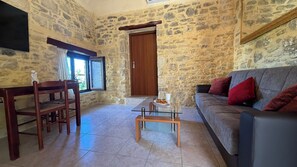 Um quarto com paredes de pedra, uma porta de madeira, um sofá, uma mesa e uma cadeira.