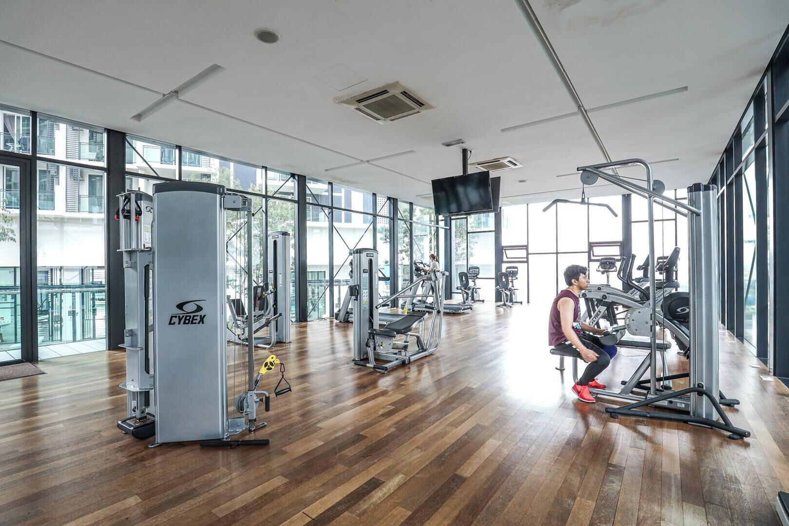 Ginásio com máquinas de cardio, equipamentos de musculação e uma ampla parede com janelas que oferece iluminação natural.