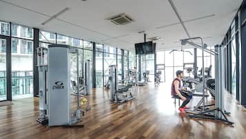 Ginásio com máquinas de cardio, equipamentos de musculação e uma ampla parede com janelas que oferece iluminação natural.