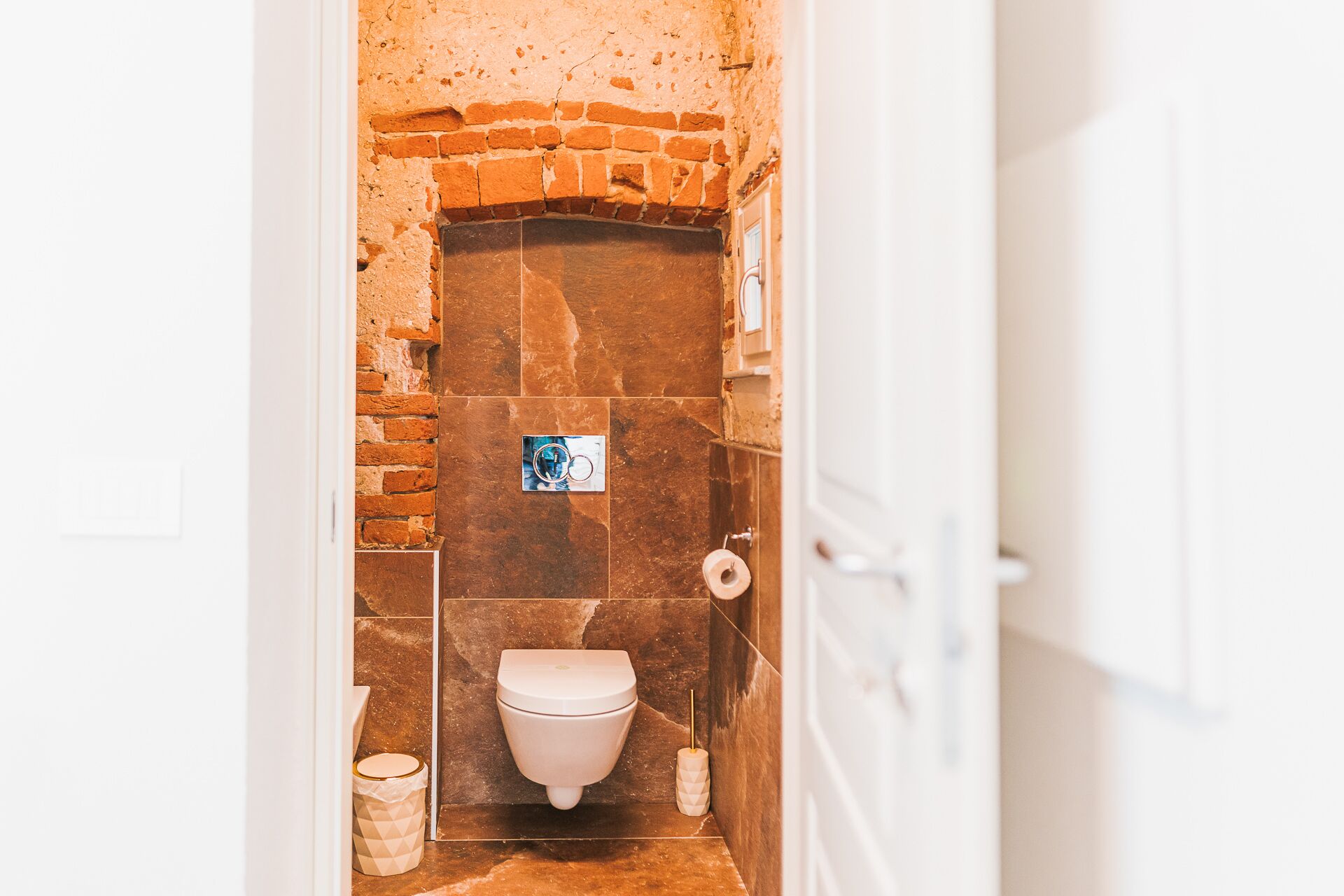 Um banheiro pequeno com parede de tijolos, vaso sanitário branco e chão revestido de mármore.