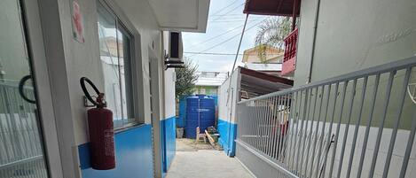 Um corredor com piso ladrilhado, um extintor de incêndio e um reservatório azul ao fundo.