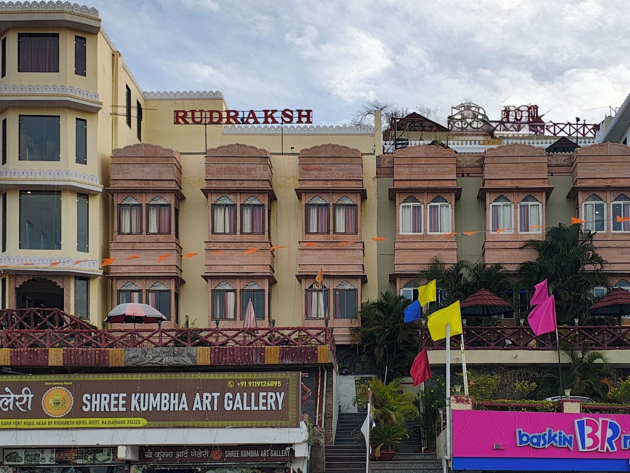 Um hotel chamado 'RUDRAKSH', com uma placa, uma galeria de arte nas proximidades e uma escadaria que leva à entrada.