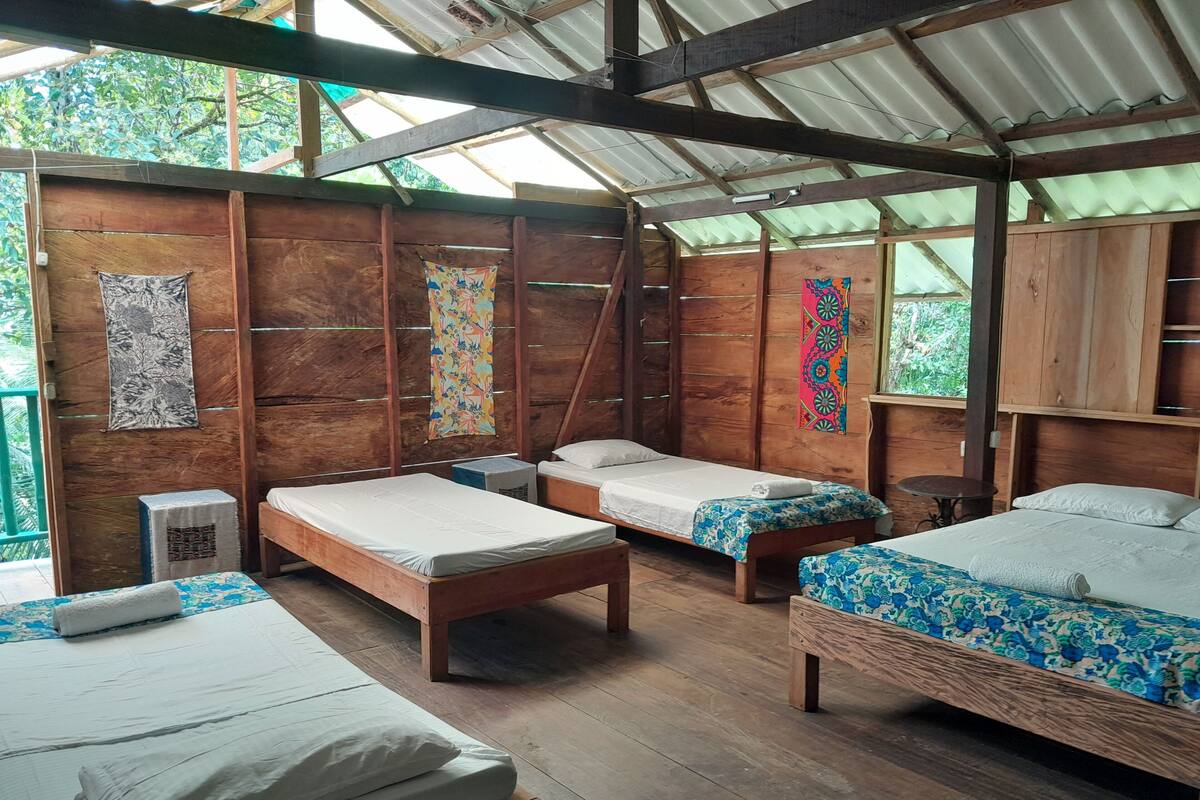 Uma cabana rústica de madeira com quatro camas simples, uma mesa pequena e um banco.