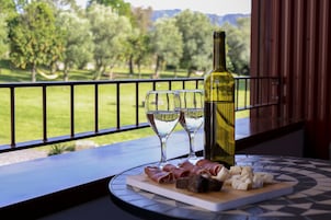 Uma mesa com uma garrafa de vinho, duas taças e um prato de comida numa varanda com vista para uma paisagem verde.
