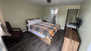 Um quarto com uma cama, uma cadeira, uma escrivaninha de madeira e uma televisão.