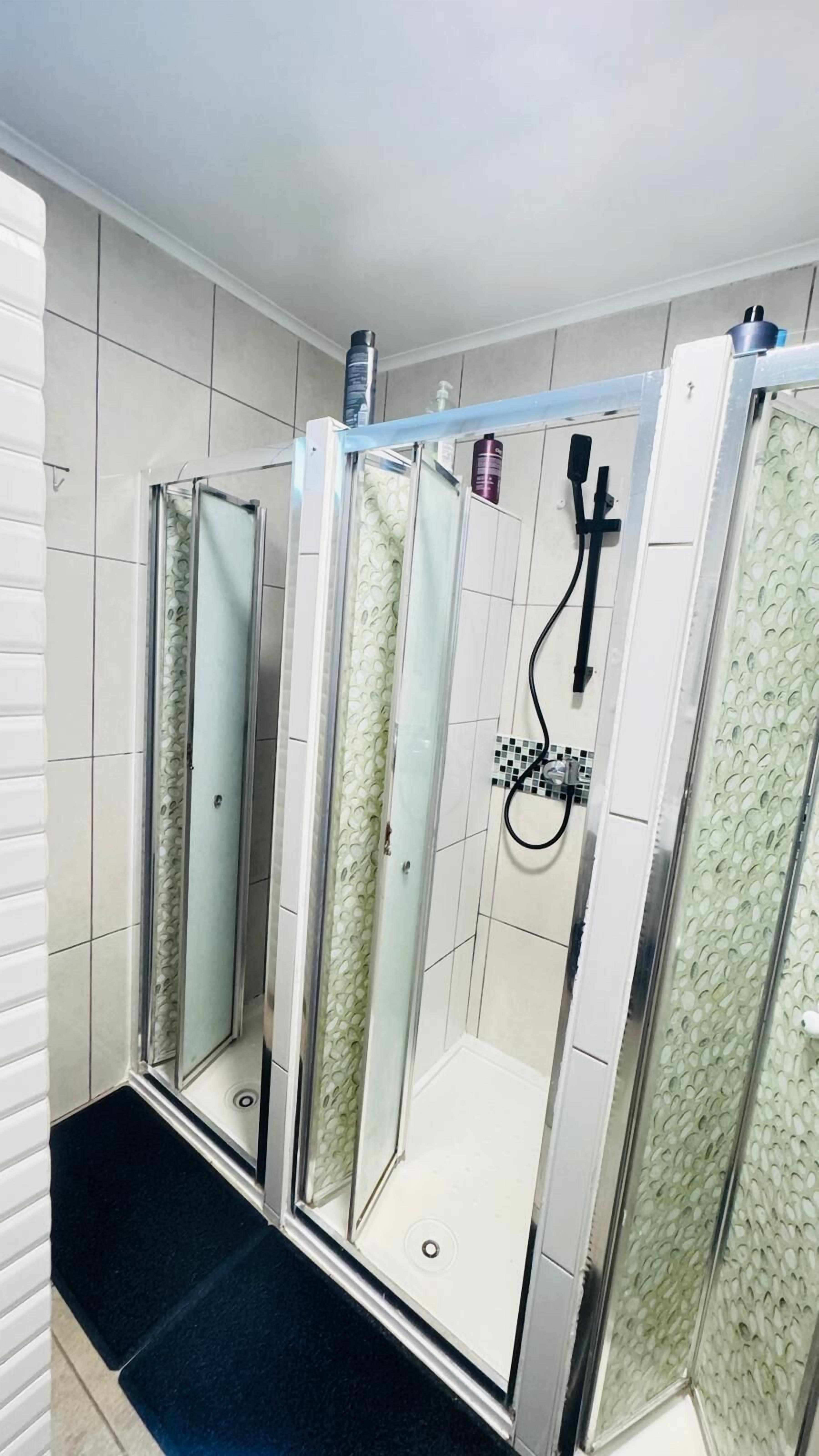 Um chuveiro sem barreiras com portas de vidro, paredes revestidas de azulejos brancos e um tapete preto na entrada.