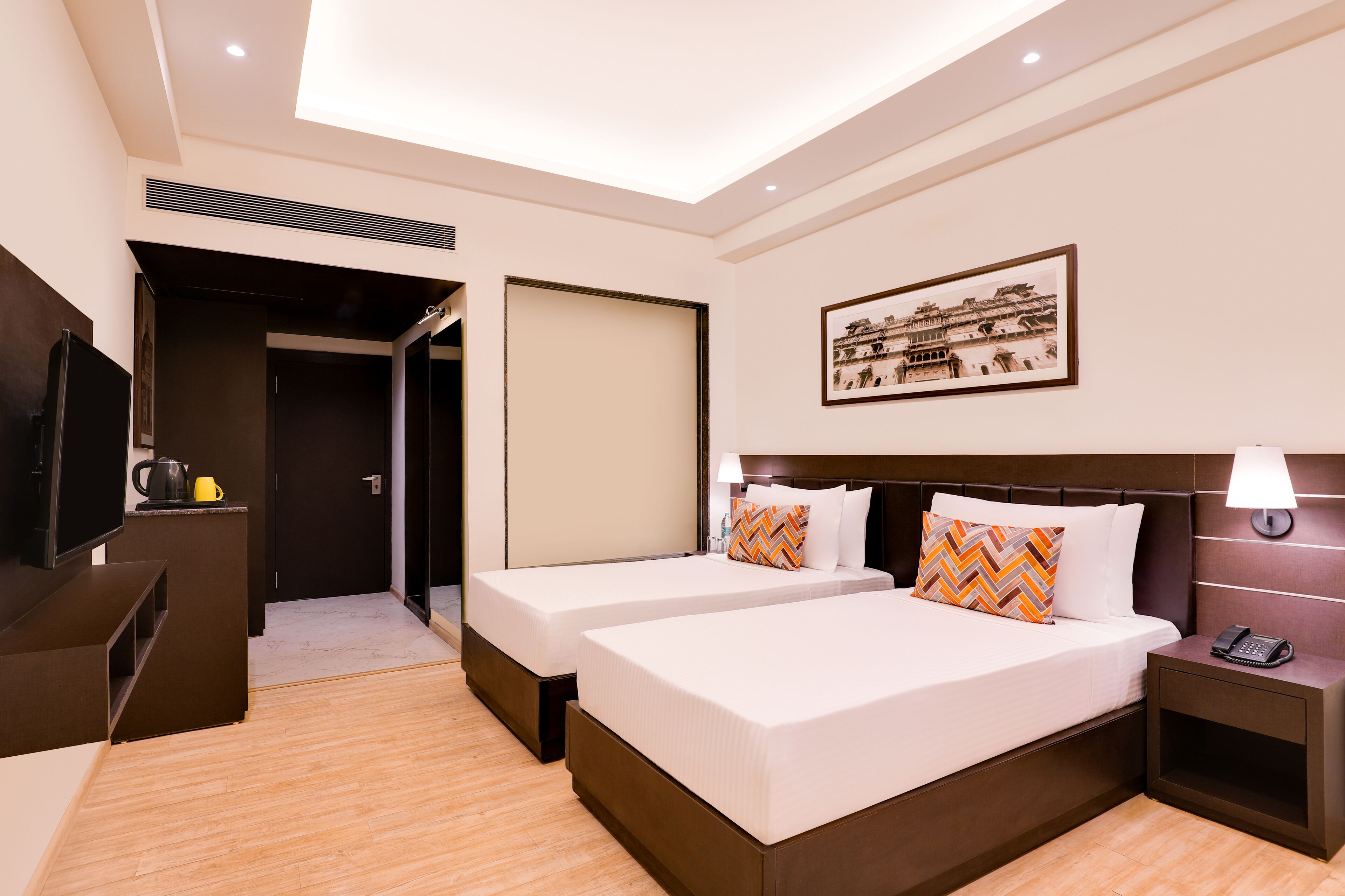 Quarto de hotel com duas camas, televisão, cafeteira e um quadro pendurado na parede.