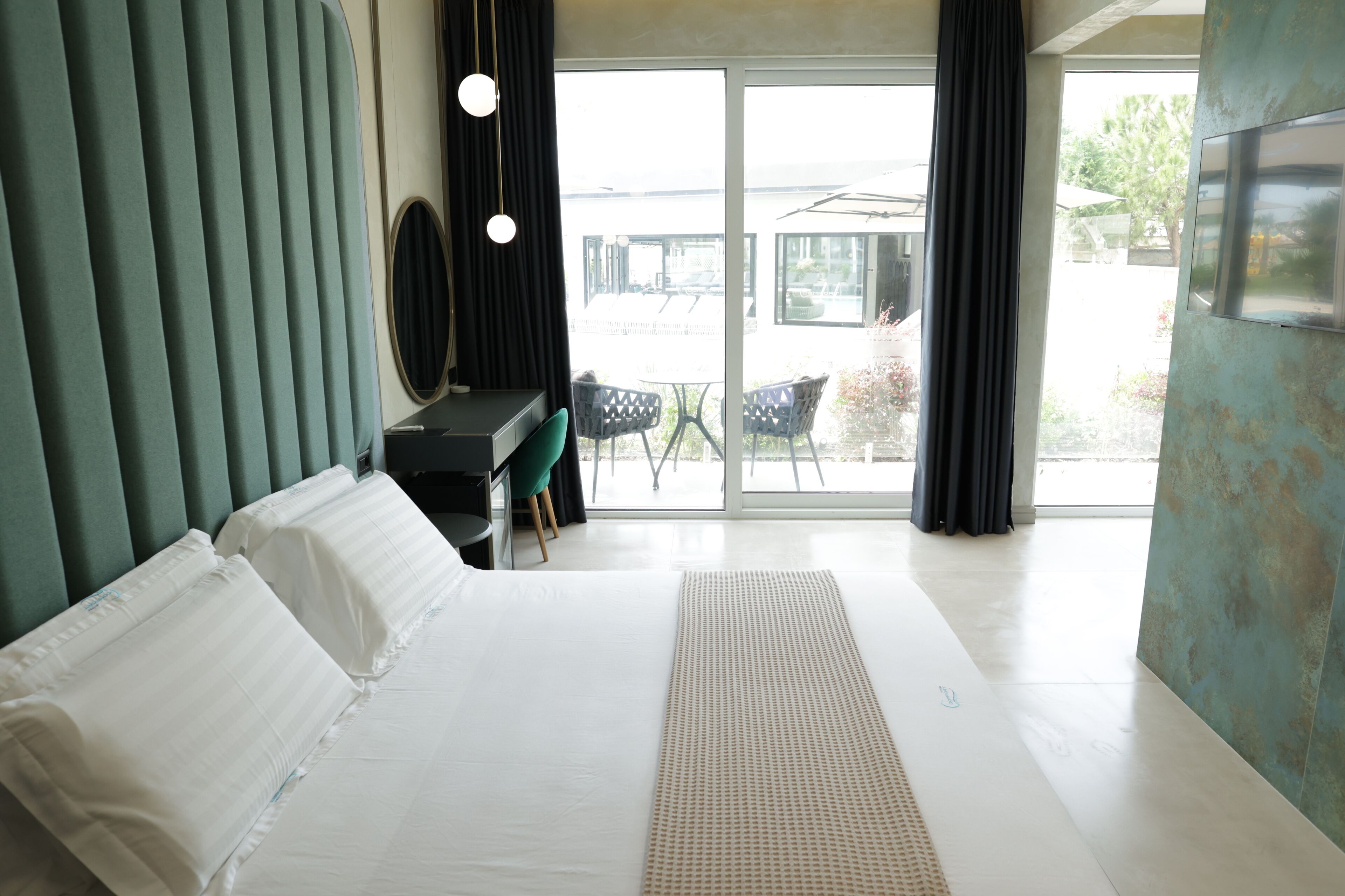 Quarto de hotel moderno com uma cama grande, uma escrivaninha e vista para o pátio externo.