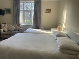 Quarto de hotel com duas camas, um sofá, uma janela com cortinas e uma luminária.