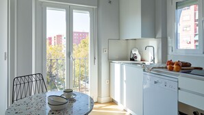 Cozinha compacta com área de refeições, máquina de lavar louça e vista para a cidade pela janela.