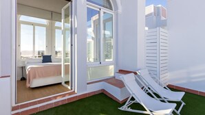 Quarto com cama, janela e varanda com cadeiras de lounge brancas.