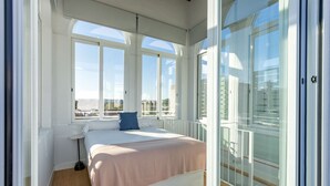 Quarto com cama grande, mesa de cabeceira e janela com vista para a cidade.
